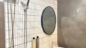 Casa de banho com parede revestida a azulejos brancos, lavatório preto, espelho e chuveiro manual.