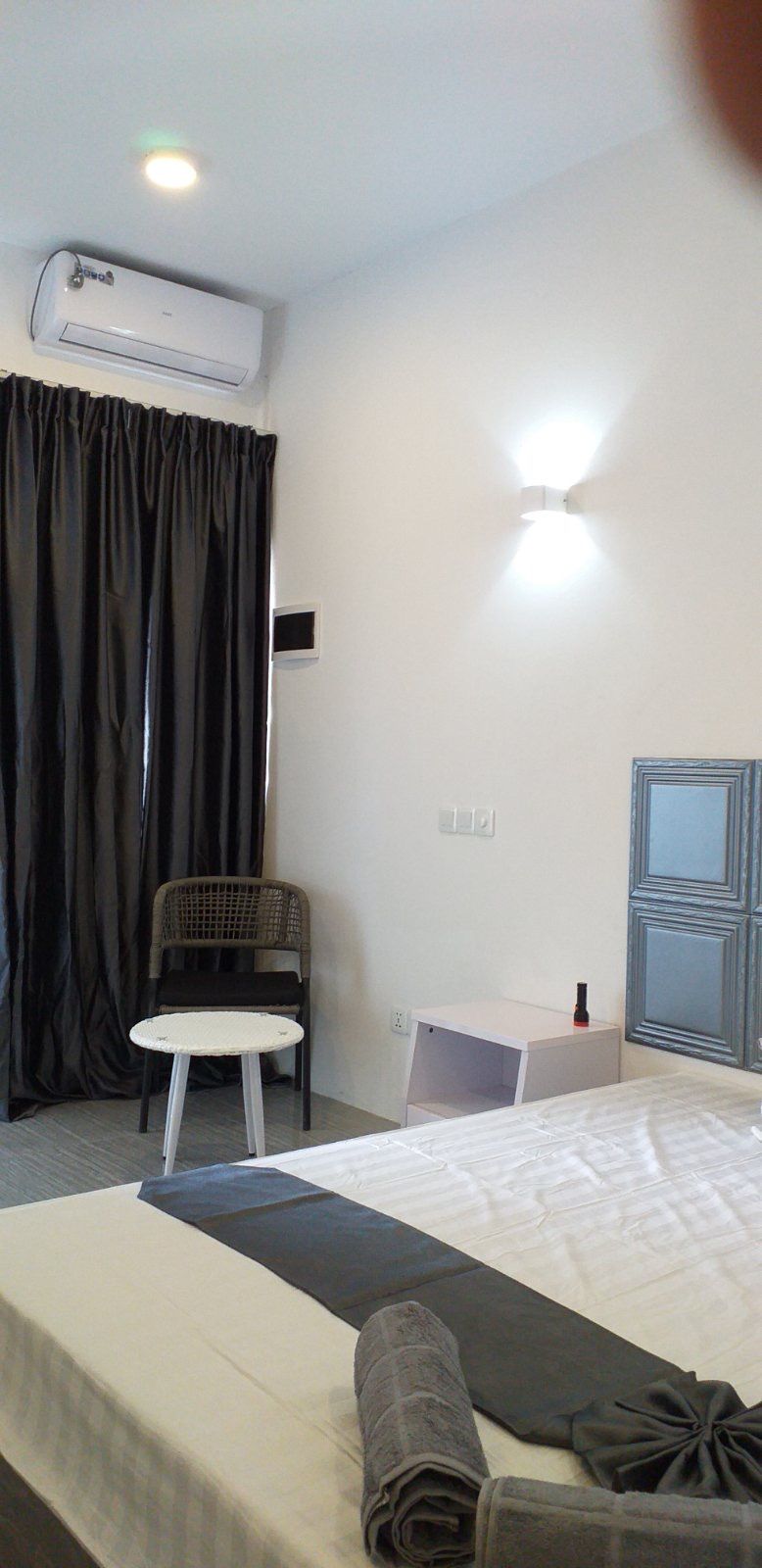 Quarto de hotel com cama, uma cadeira, uma mesinha, ar condicionado e luminária na parede.