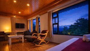 Quarto com cama, poltrona de balanço, televisão e janela com vista.