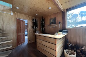 Interior em madeira com bancada de cozinha, espaço para vinhos e um quadro na parede.