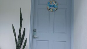Uma porta azul clara com um arranjo de boas-vindas, um vaso de planta e um interruptor na parede.