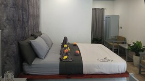 Quarto de hotel moderno com cama grande, roupa de cama cinza e branca, cabeceira cinza, uma pequena mesa com uma planta e um espelho.