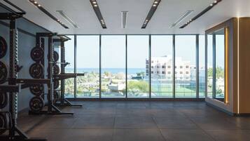 Uma academia com equipamentos de musculação e amplas janelas que oferecem vista para o mar e edifícios.