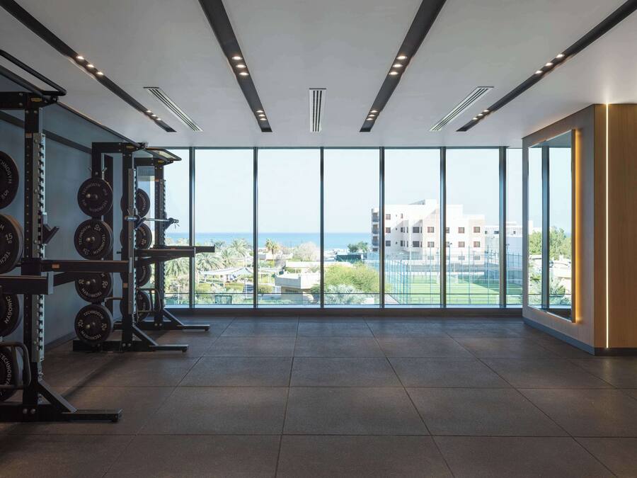 Uma academia com equipamentos de musculação e amplas janelas que oferecem vista para o mar e edifícios.