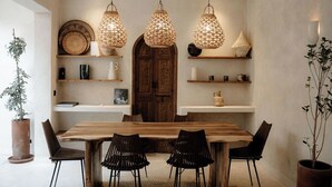 Uma sala de jantar com mesa e cadeiras de madeira, luminárias de vime pendentes e prateleiras com objetos decorativos.