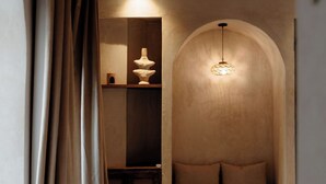 Quarto com teto de madeira, cama, mesa de cabeceira, luminária e prateleira na parede com objetos decorativos.