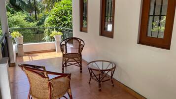 Uma varanda com móveis de vime, uma mesa de vidro e vista para o verde exuberante.