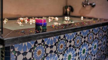 Paredes azulejadas com padrão floral, pequenas pilhas de velas coloridas e confetes espalhados.
