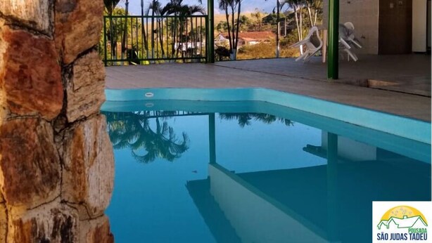 Uma piscina com muro de pedra, área de varanda coberta e palmeiras ao fundo.