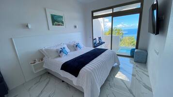 Quarto com uma cama, televisão, quadro e vista para o oceano.