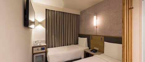 Quarto de hotel com duas camas, uma TV de tela plana, mesa de cabeceira com telefone, abajur e espelho fixado na parede.