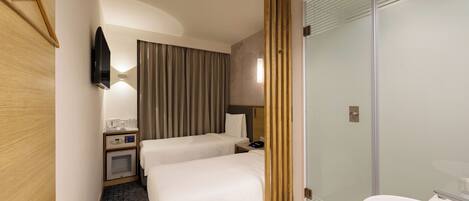 Quarto de hotel com duas camas, uma mesa de cabeceira com abajur, um armário pequeno e área de chuveiro com porta de vidro.