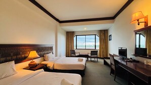 Quarto de hotel com duas camas, uma escrivaninha com computador, uma cadeira e uma janela grande com vista.