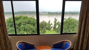 Quarto com uma grande janela com vista para um rio, duas poltronas estofadas em azul e uma mesa de madeira.