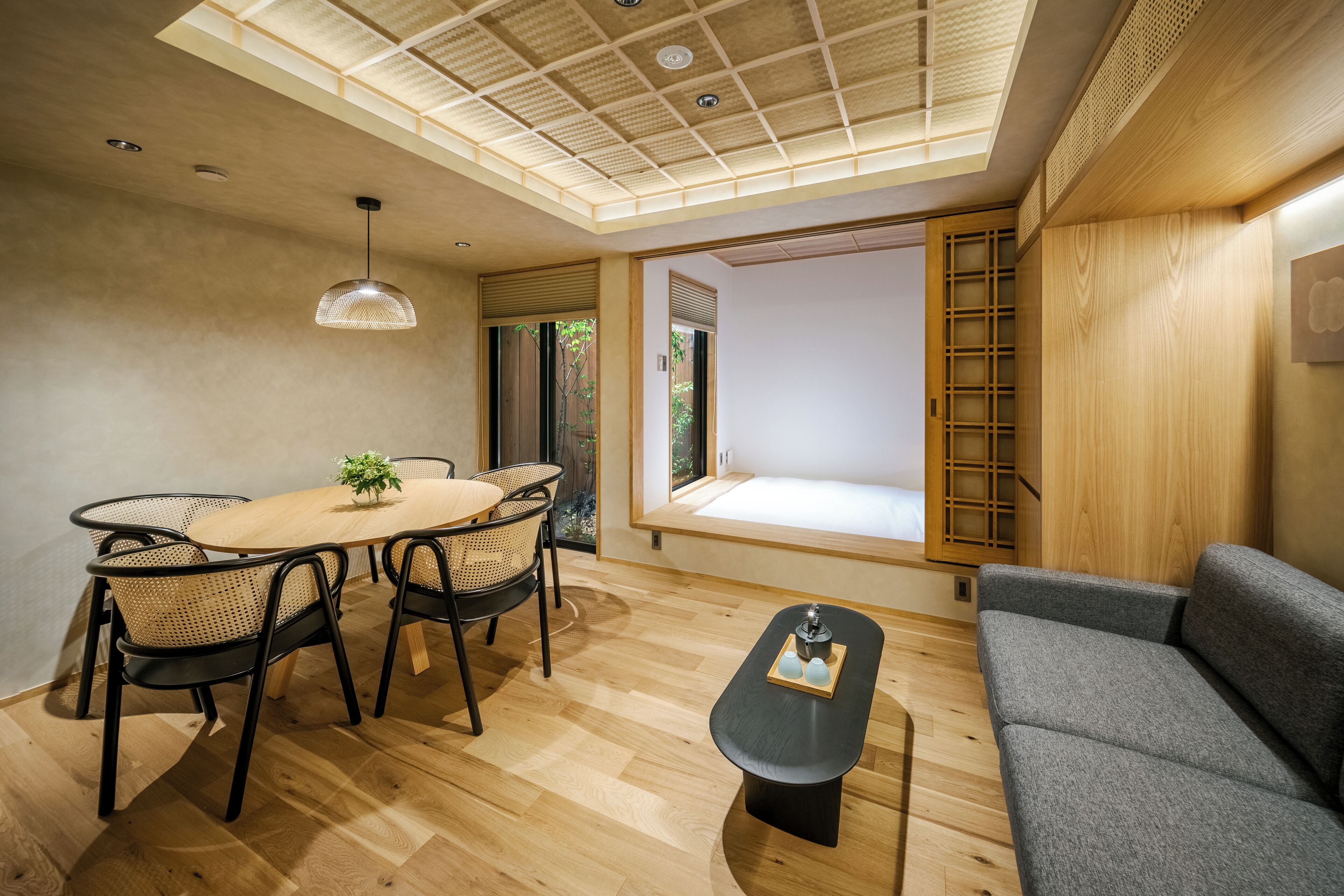 Uma sala de estar moderna com uma mesa de jantar de madeira, cadeiras pretas e de vime, um sofá cinza e uma mesa de centro preta.
