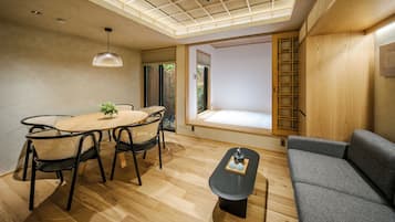 Uma sala de estar moderna com uma mesa de jantar de madeira, cadeiras pretas e de vime, um sofá cinza e uma mesa de centro preta.