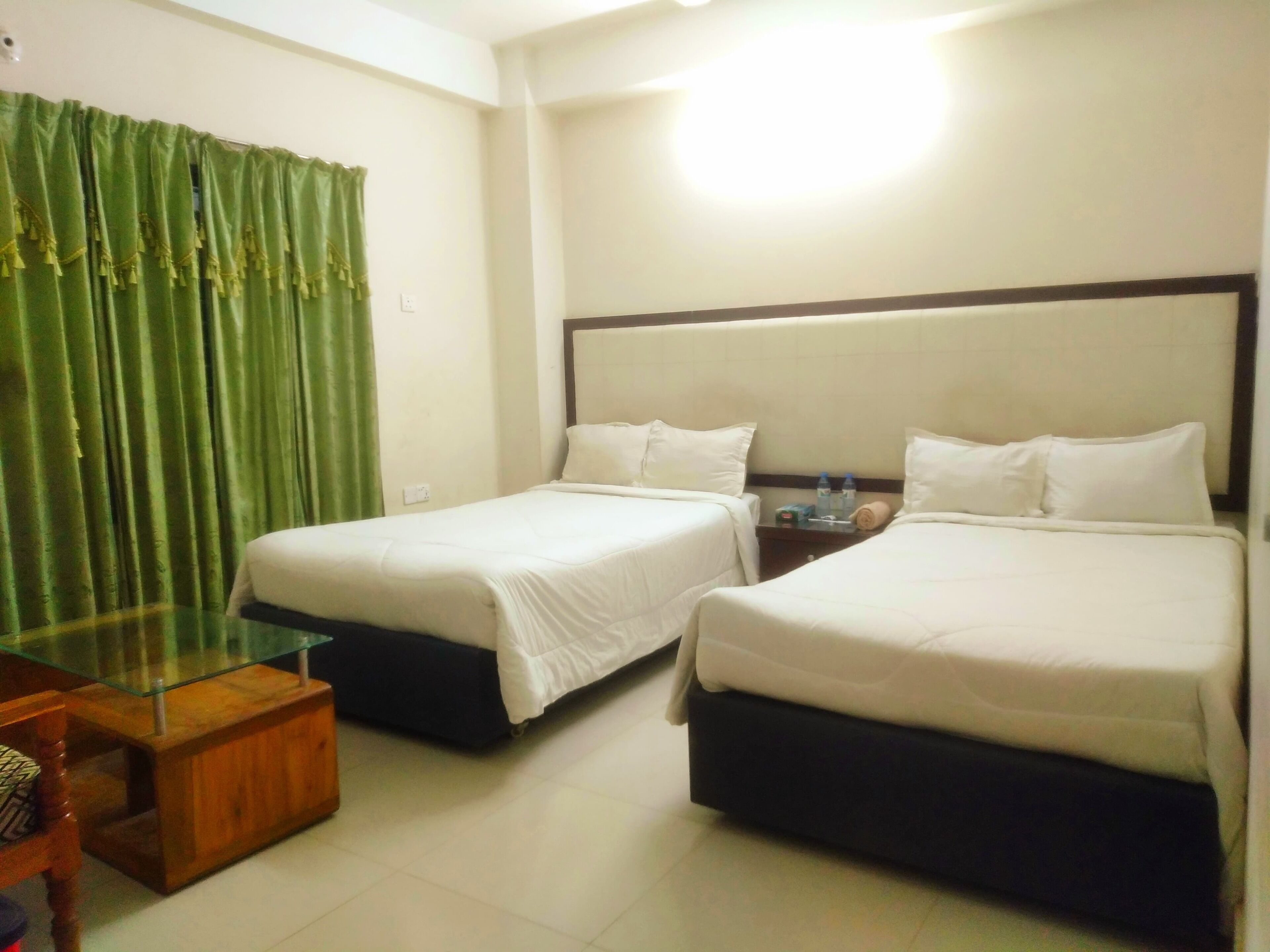 Quarto de hotel com duas camas, uma mesinha de madeira e uma mesa com tampo de vidro.