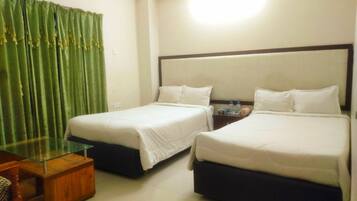 Quarto de hotel com duas camas, uma mesinha de madeira e uma mesa com tampo de vidro.