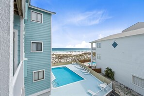 Piscina com espreguiçadeiras, vista para a praia e um edifício com varanda.