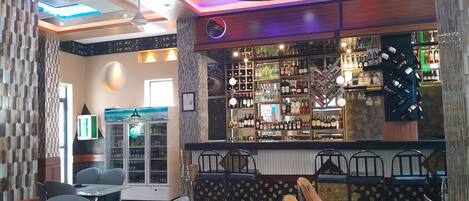 Uma área de bar com diversas opções de assento, incluindo mesas e cadeiras, e um bar bem abastecido com inúmeras garrafas.
