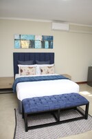 Quarto bem arrumado com cama, um banco e ar condicionado fixado na parede.