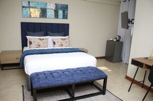 Quarto bem organizado com cama, banco, escrivaninha e um pequeno armário.