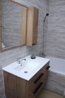 Casa de banho moderna com toucador de madeira, lavatório branco, espelho e chuveiro.