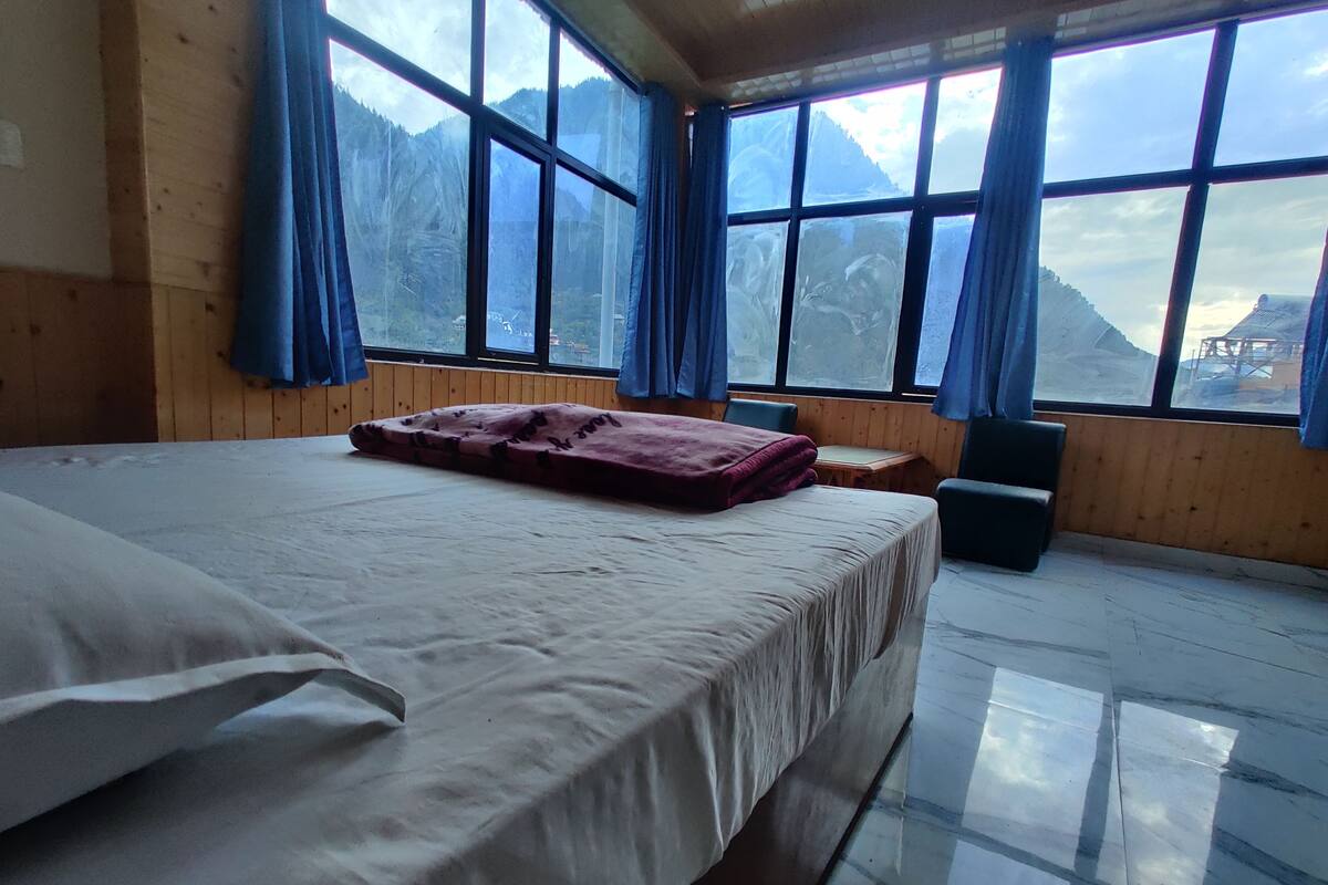 Quarto com cama, piso de madeira, janela e vista para as montanhas, além de uma mesa pequena.