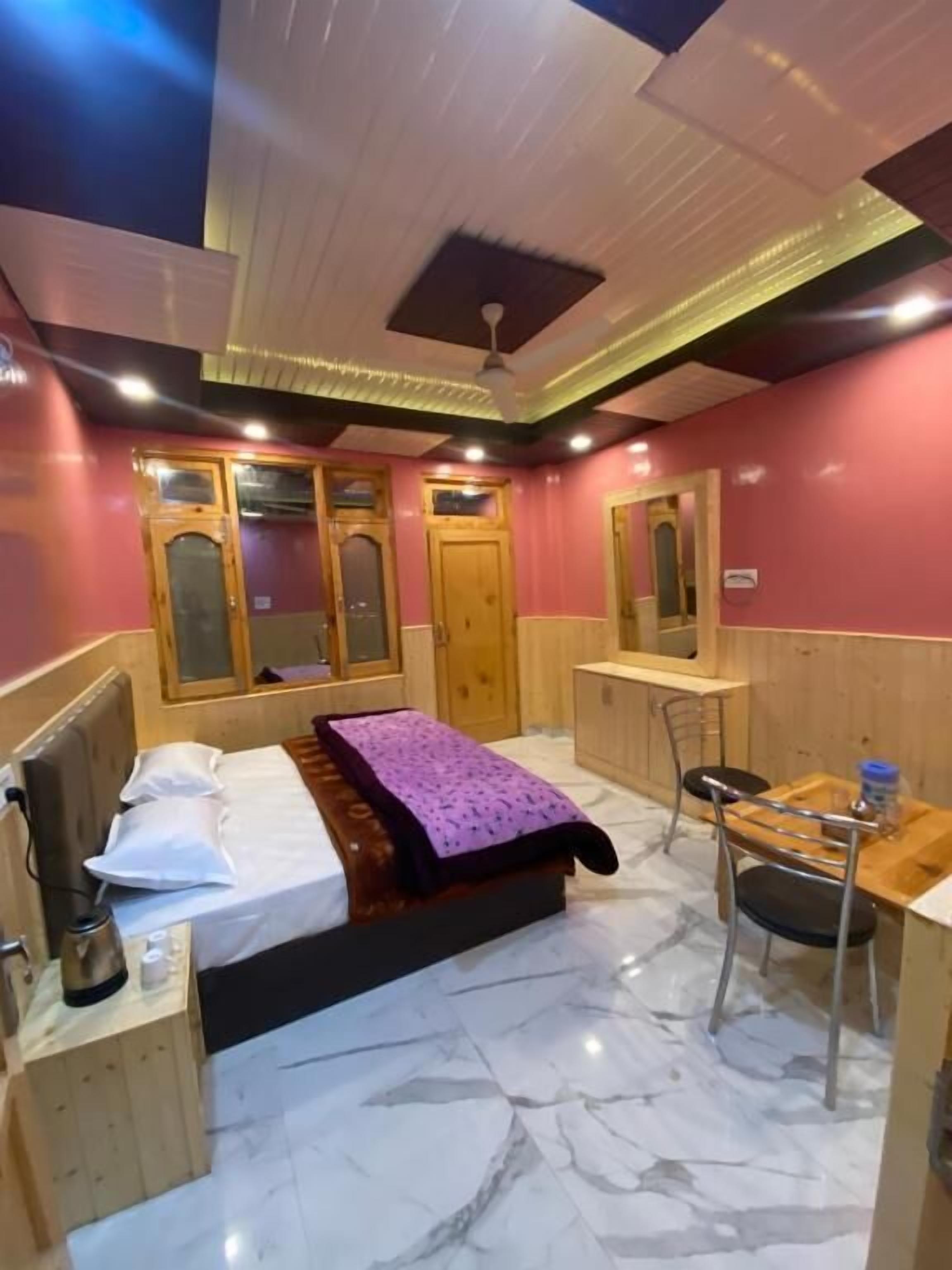 Quarto de hotel com cama, escrivaninha, cadeira e espelho.