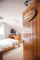 Quarto com porta de madeira, uma cama, mesa de cabeceira, cômoda e televisão.