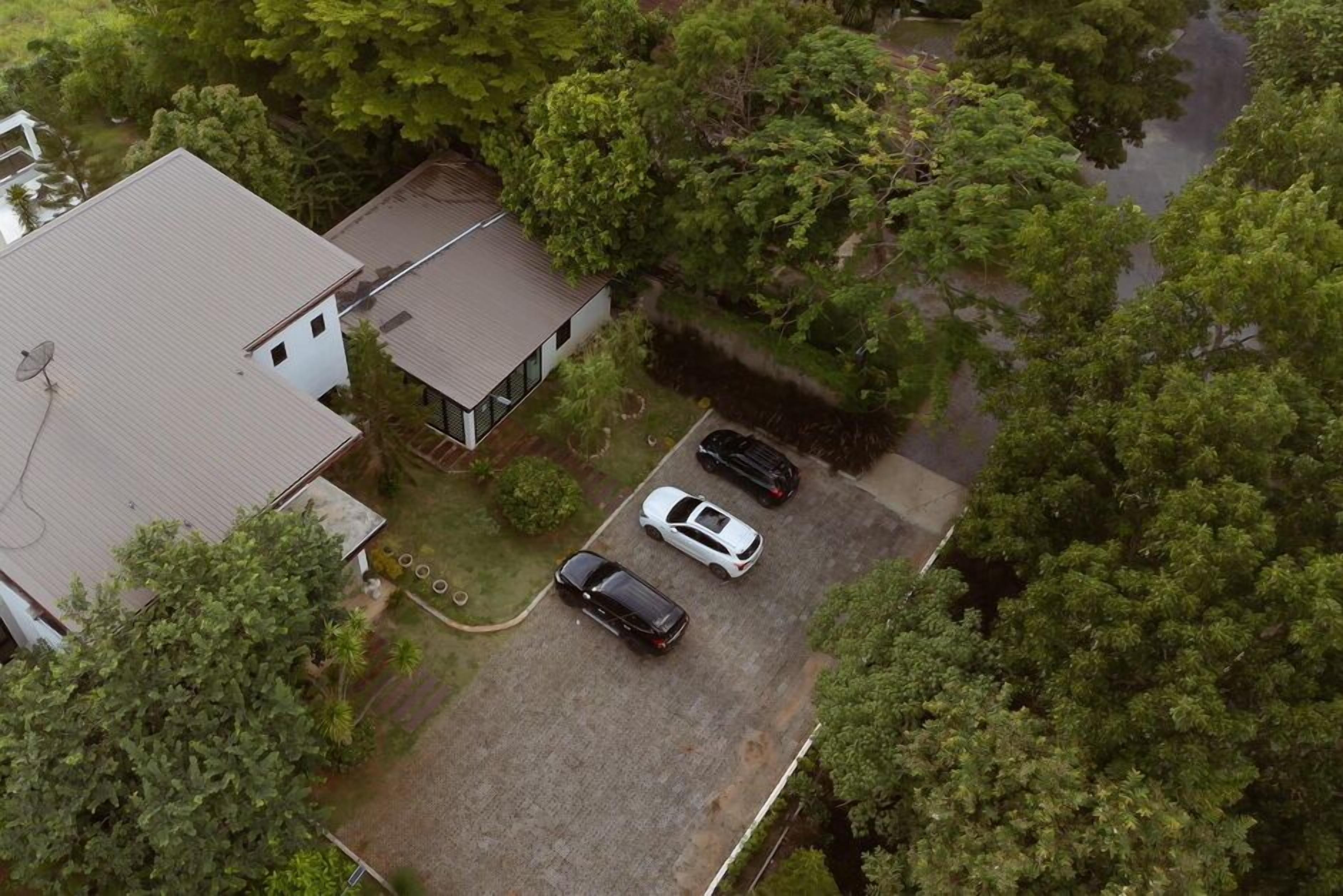 Vista aérea de uma propriedade residencial com uma casa, entrada para carros e dois veículos estacionados.