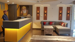Uma área de recepção de hotel com balcão, um sofá com almofadas 'PLAYOTEL' e um aplique de parede.