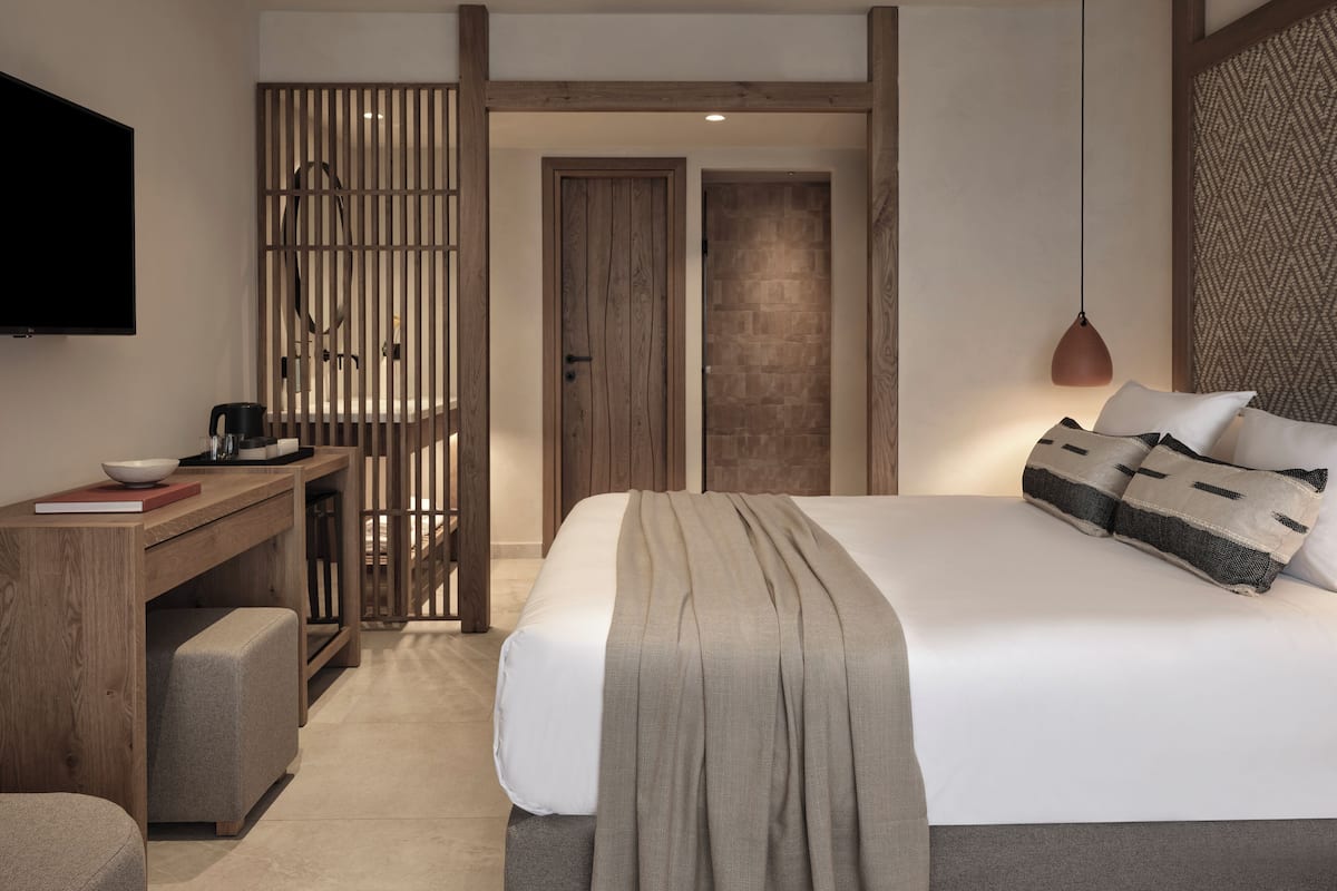 Quarto de hotel moderno com uma cama grande, uma escrivaninha com máquina de café, TV e parede estampada.
