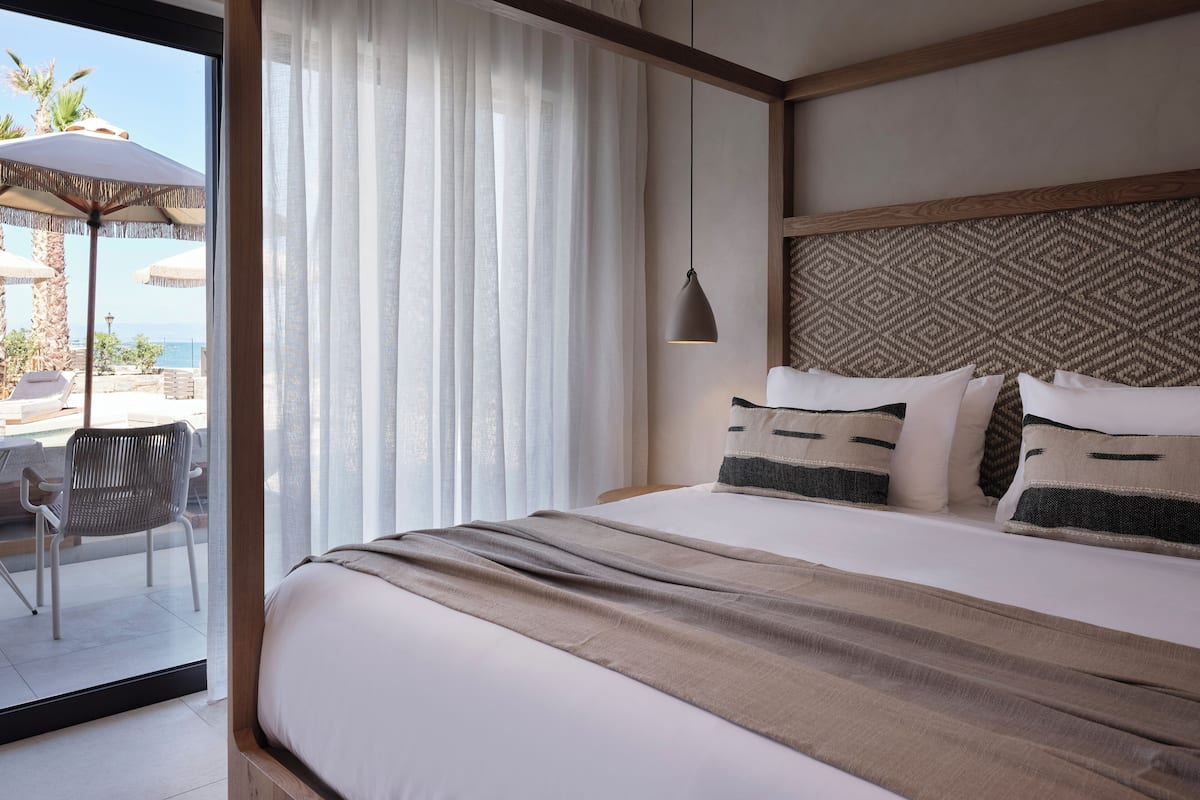 Quarto de hotel com uma cama grande, vista para o mar, varanda com área de estar e cabeceira estampada.