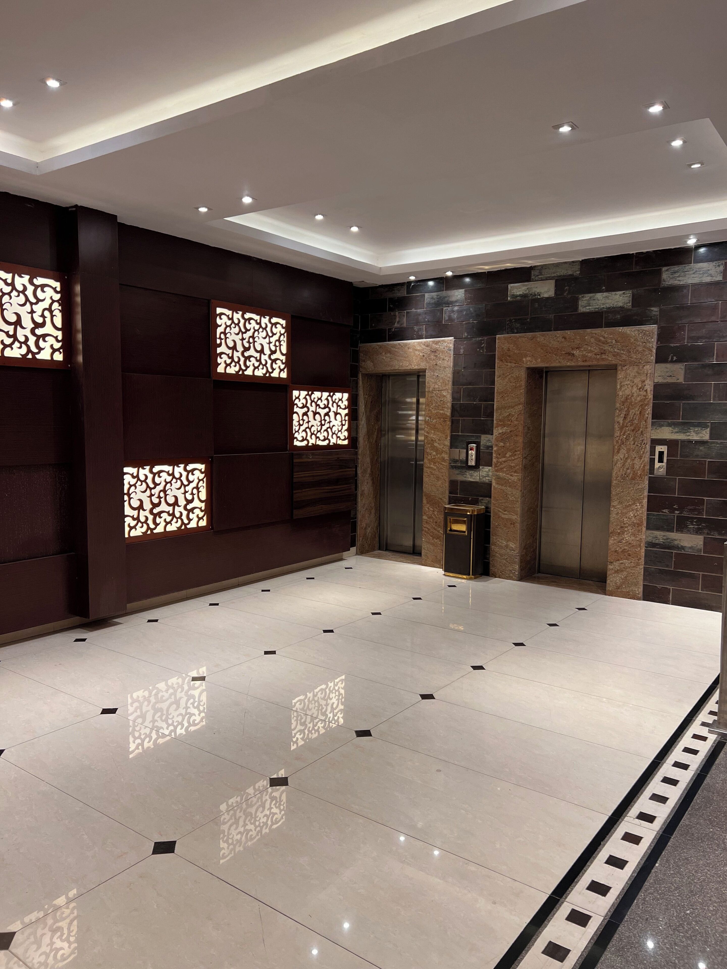Um hall amplo com piso de azulejos brilhante, dois elevadores e painéis decorativos na parede.