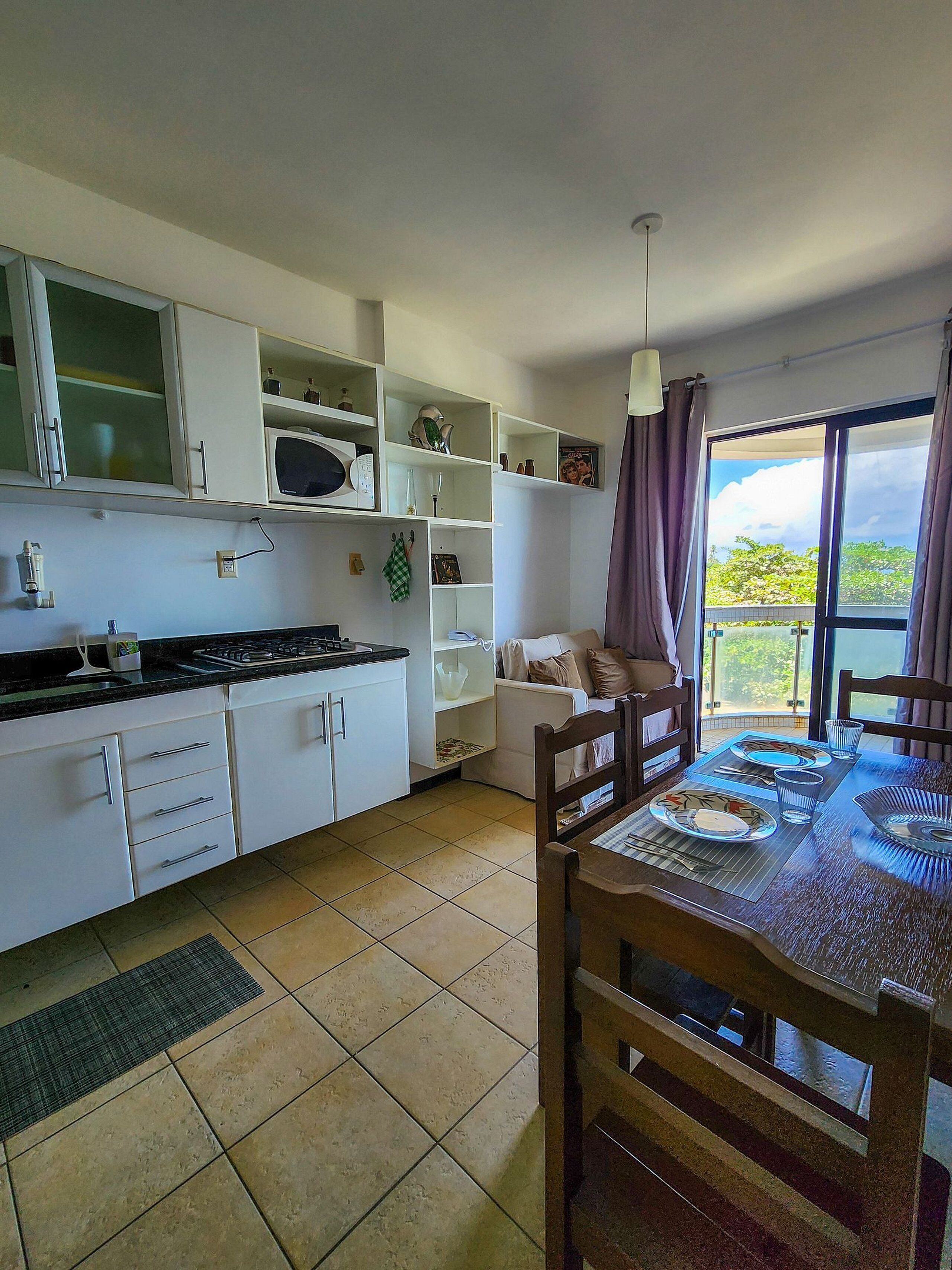 Uma cozinha com armários brancos, micro-ondas e uma área de jantar com mesa posta para quatro pessoas.