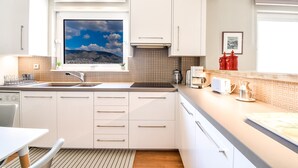 Uma cozinha moderna com armários brancos, uma janela embutida com vista para a cidade, uma pia e um balcão com cafeteira e torradeira.