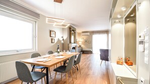 Uma sala de jantar moderna com mesa de madeira, cadeiras estofadas cinzas e iluminação pendente.