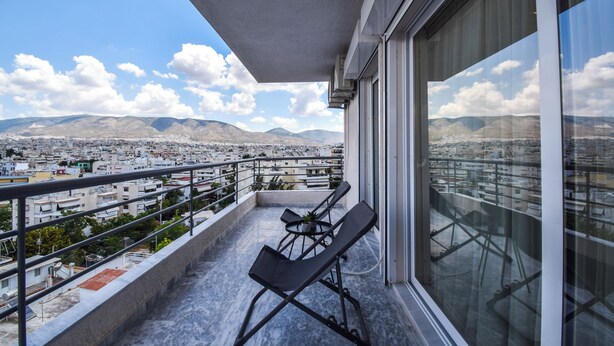 Varanda com duas cadeiras pretas e uma mesa pequena, com vista para um horizonte urbano e montanhas ao longe.