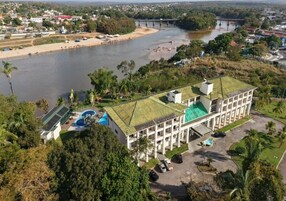 Um hotel grande com piscina, situado perto de um rio e uma ponte ao fundo.