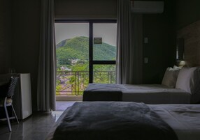 Quarto de hotel com varanda, duas camas, uma cadeira e vista para uma paisagem montanhosa.