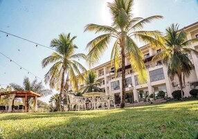 Um hotel com área de estar coberta ao ar livre, palmeiras e um edifício com vários andares e varandas.