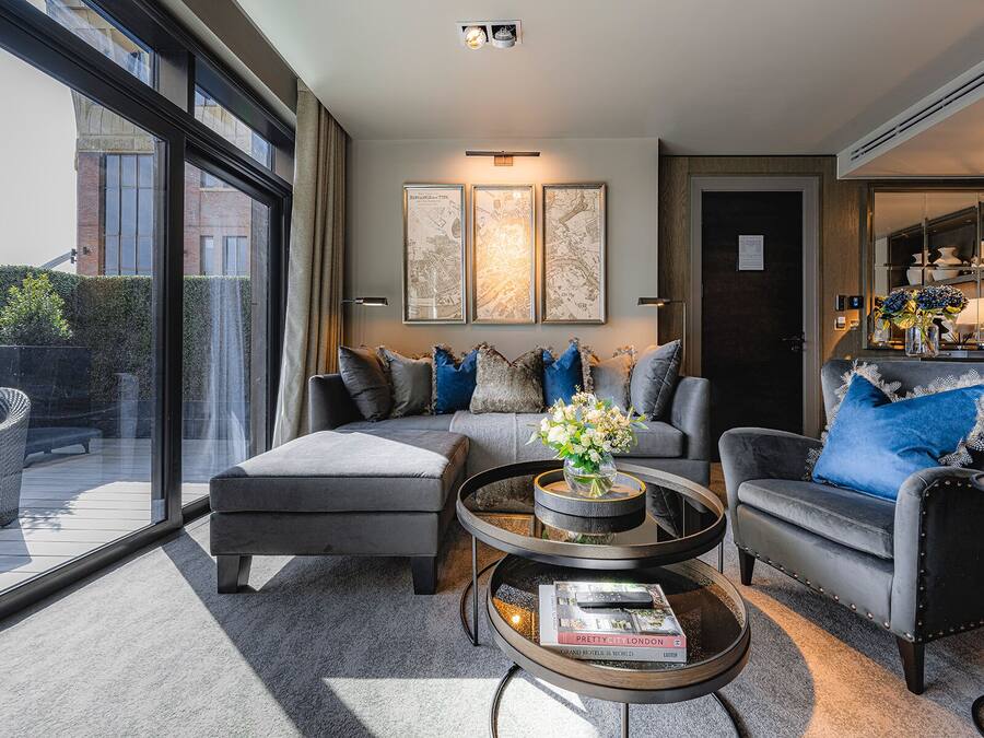 Uma sala de estar moderna com um sofá cinzento, uma mesa de centro redonda com um livro e vista para o horizonte urbano através de grandes janelas.