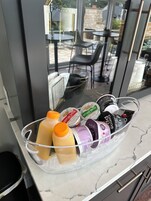 Recipiente de vidro sobre uma bancada com diversos alimentos, incluindo garrafas e potes de queijo cottage, iogurte e outros produtos lácteos.