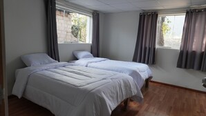 Quarto com duas camas, cortinas cinzas e piso de madeira.