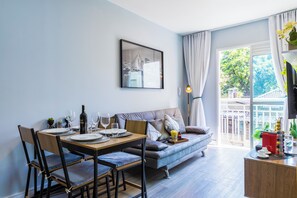 Uma sala de jantar com uma mesa posta para dois, um sofá e vista para um jardim através de uma porta de vidro.