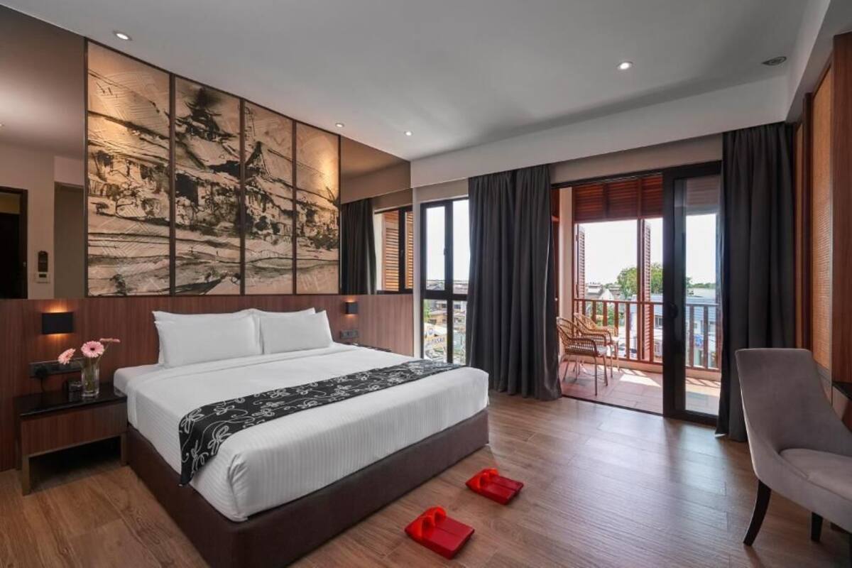 Quarto de hotel moderno com uma cama grande, vista da cidade e varanda com assentos externos.