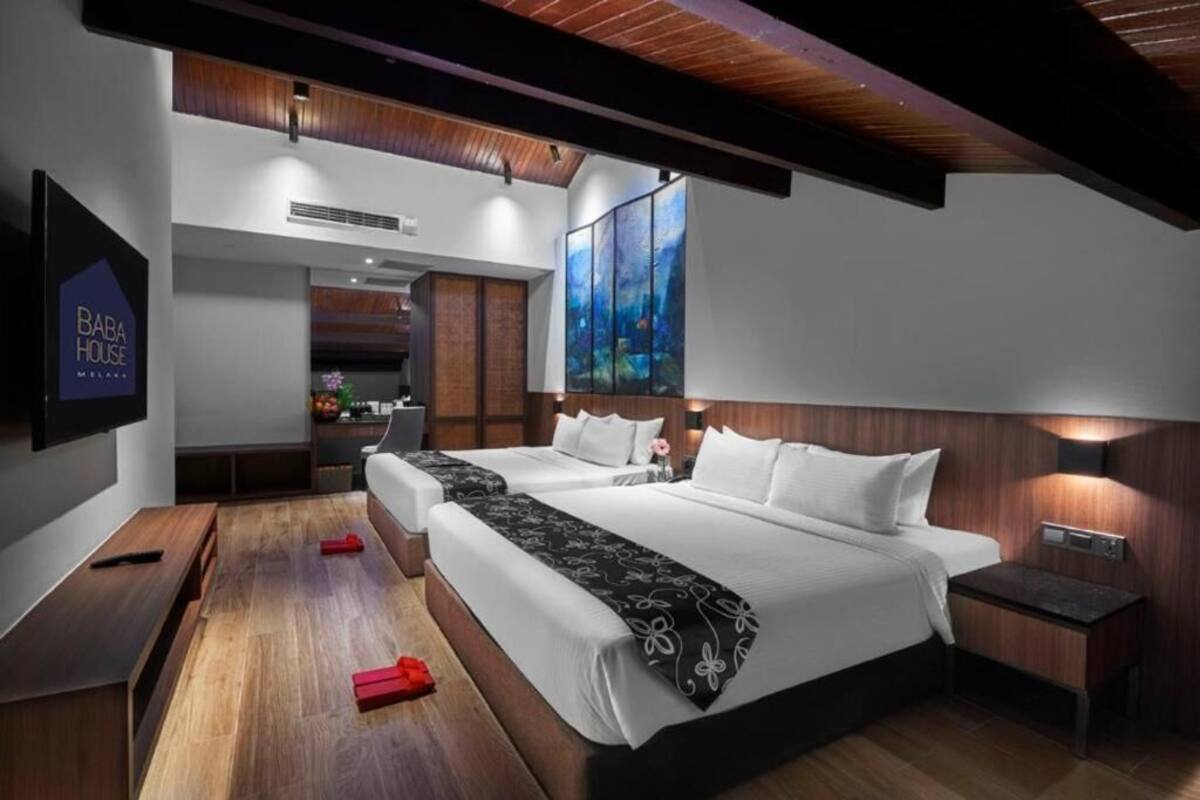 Quarto de hotel moderno com uma cama grande, televisão de tela plana, piso de madeira e um quadro na parede.