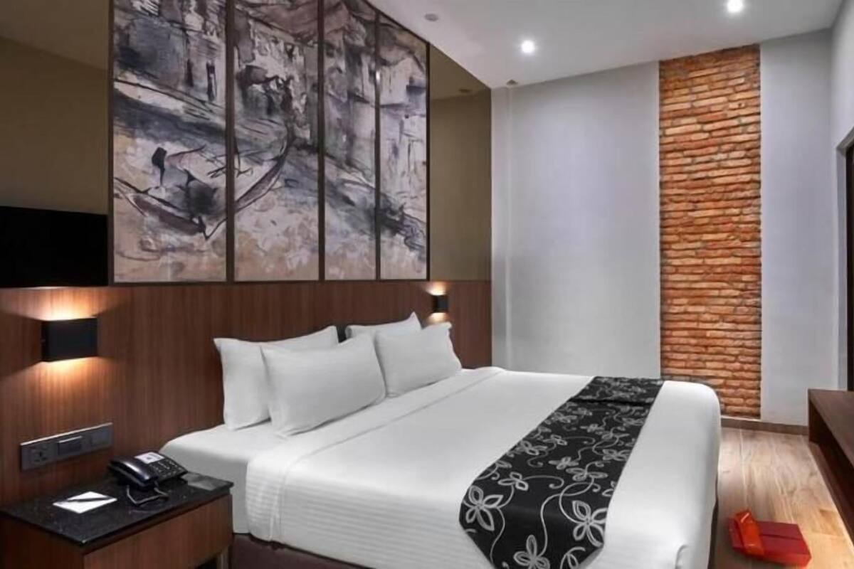 Quarto de hotel moderno com uma cama grande, televisão de tela plana, cabeceira de madeira e parede de tijolos decorativa.