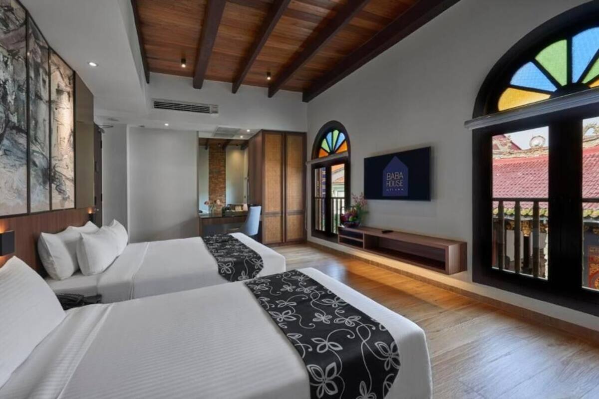 Quarto de hotel com duas camas, um grande quadro abstrato, uma janela de vitrais e vista para o exterior.